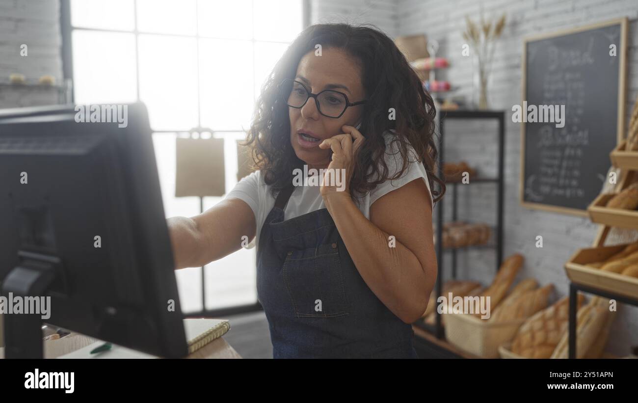 Woman talking on phone while working at computer in cozy bakery shop ...