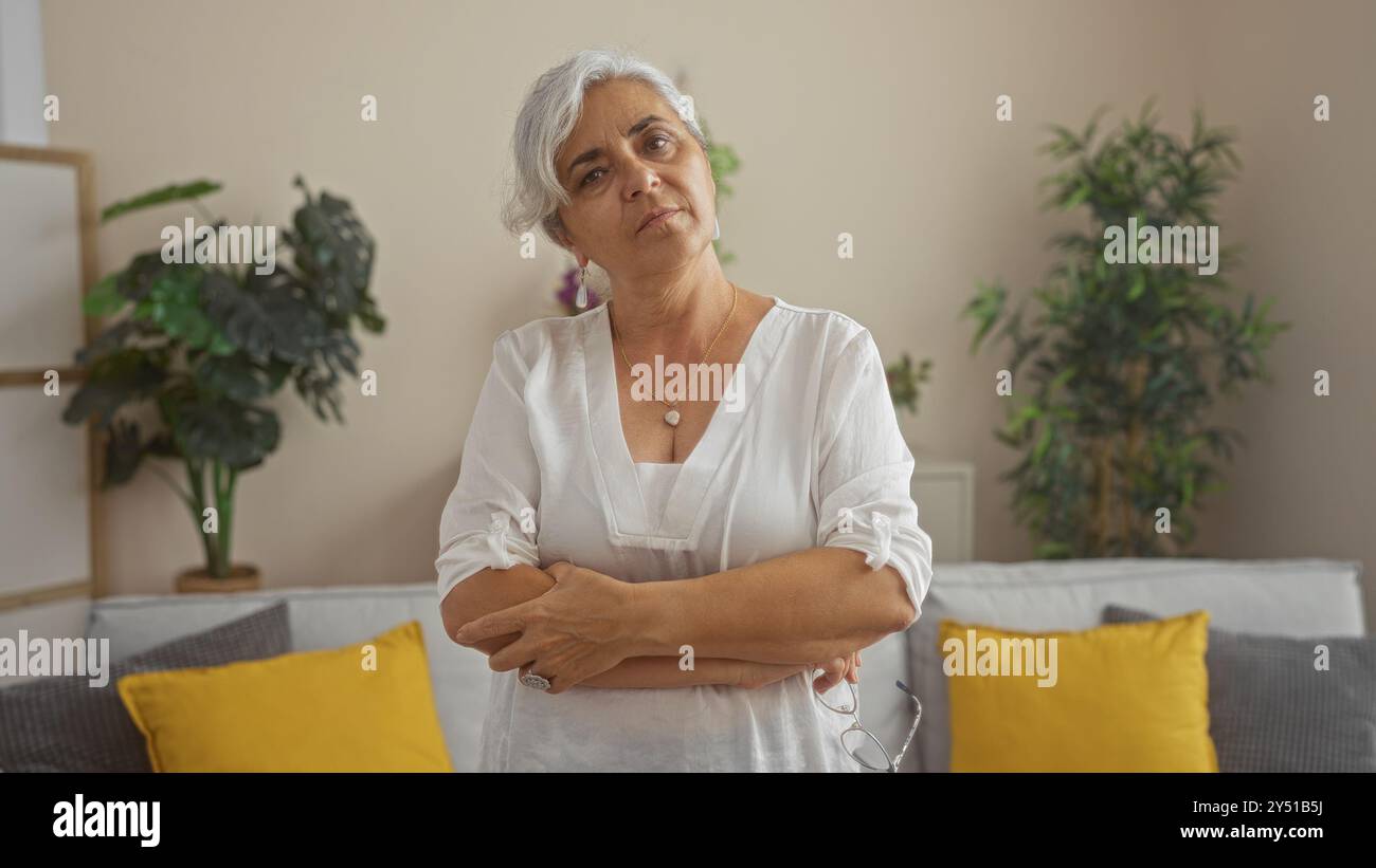 Middle-aged woman with crossed arms in a living room with plants and ...