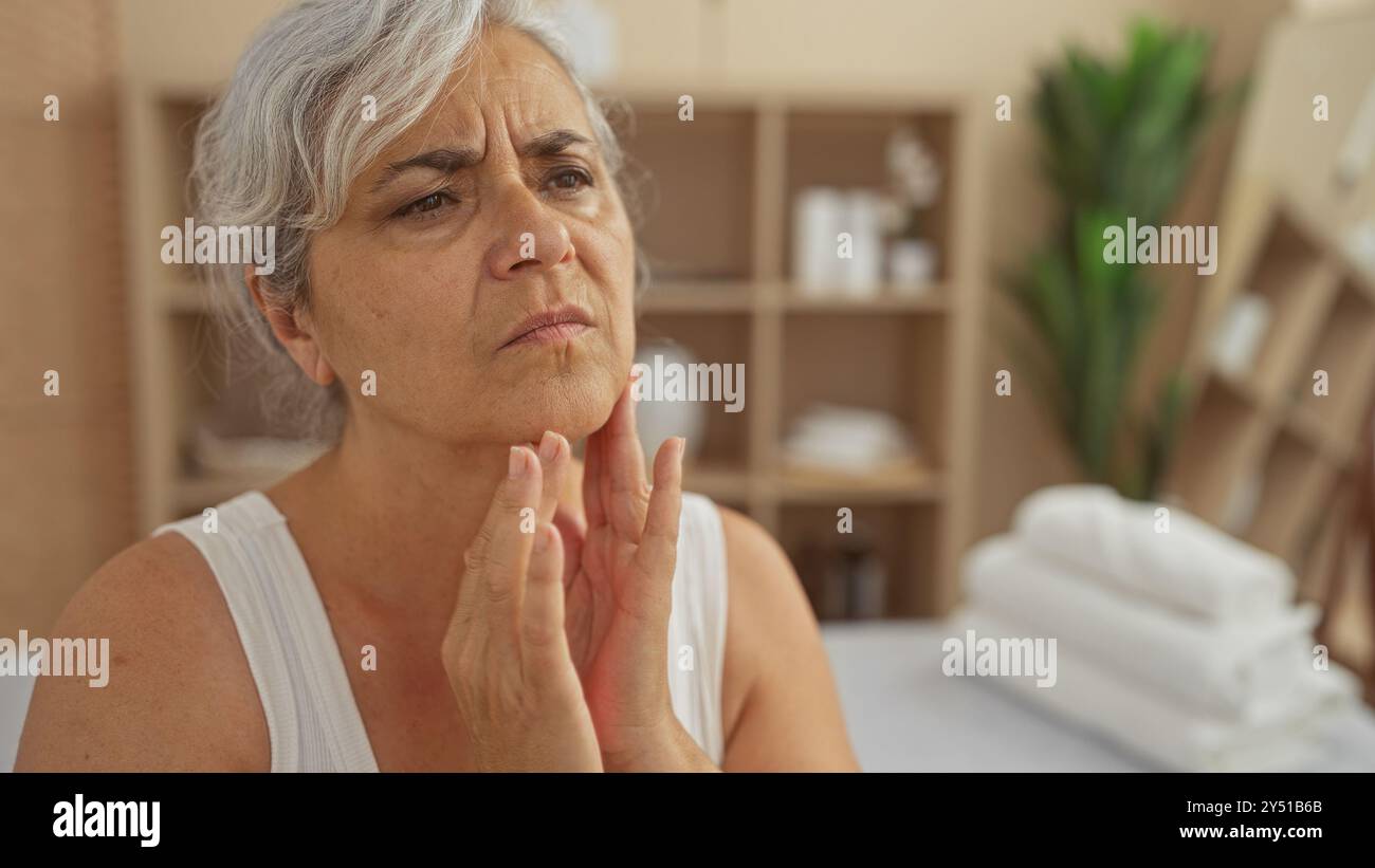 Mature woman with grey hair at a spa examining her face in a serene ...