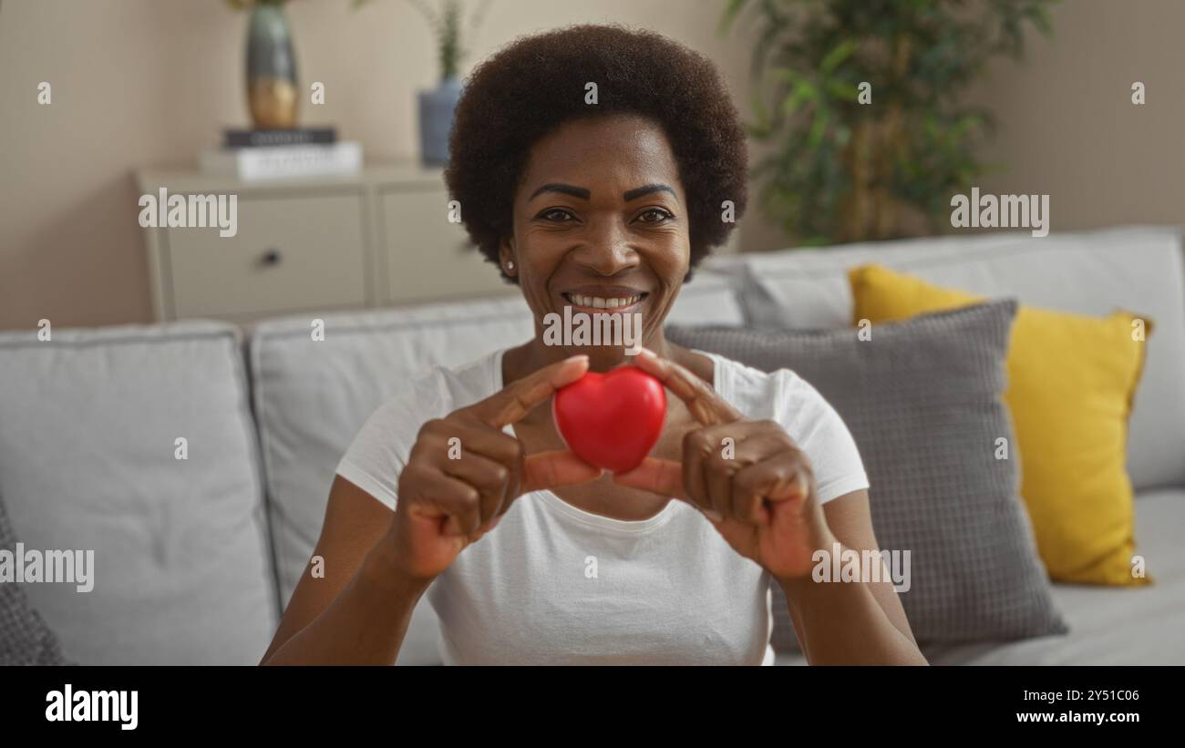Woman holding heart-shaped object sitting on sofa, wearing white shirt ...