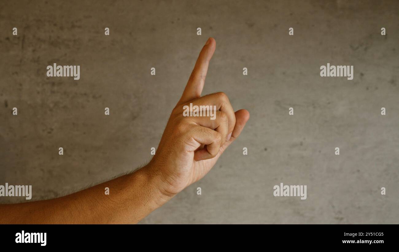 Man's hand pointing upwards against concrete background, emphasizing a ...