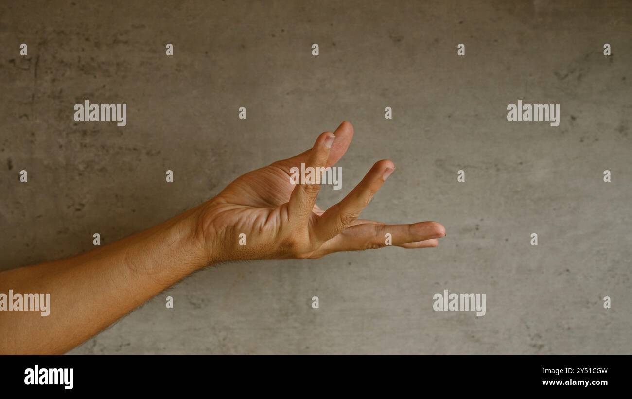 Man's hand with fingers extended against a concrete wall background ...