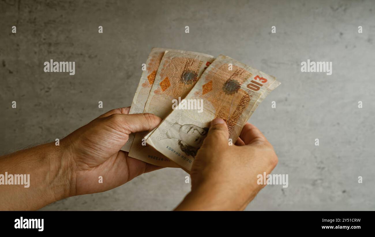 Hands holding british pounds against a concrete background, showcasing ...
