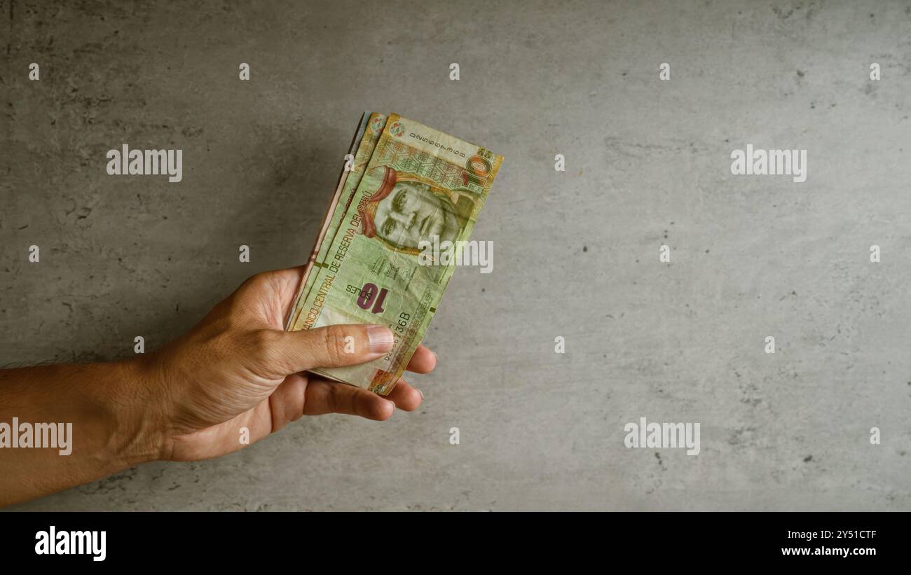 Hand holding peruvian sol bills against a concrete background ...