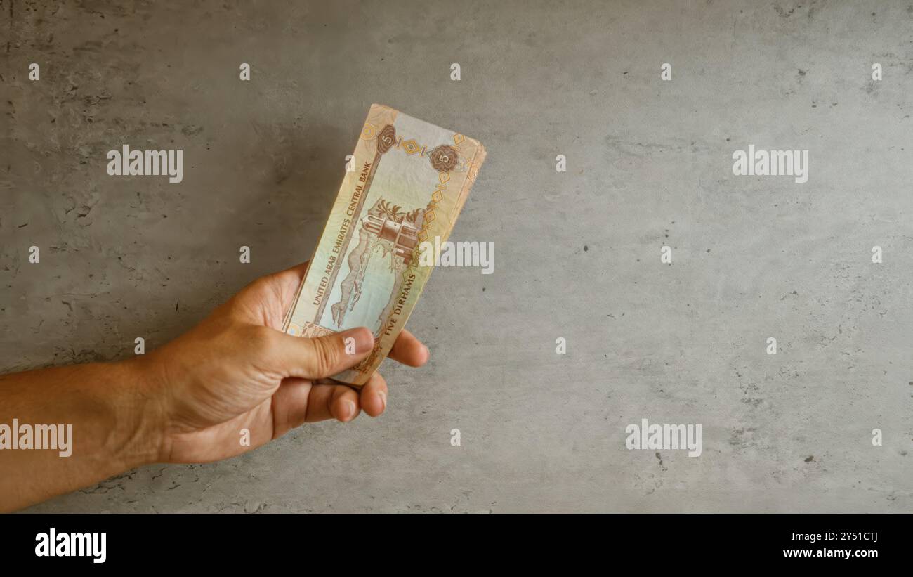 Hand holding uae dirhams against a concrete background, showcasing ...