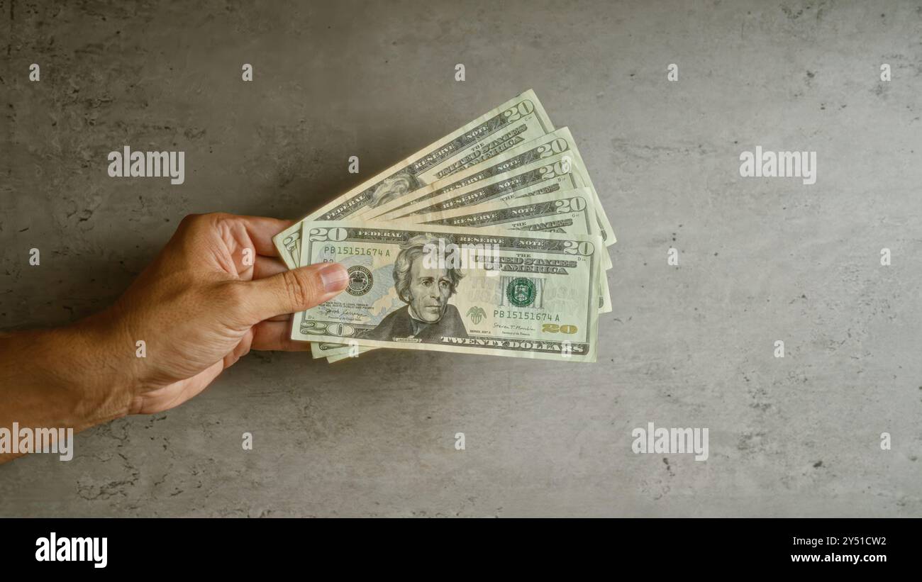 Hand holding united states dollar bills fanned out against a concrete ...