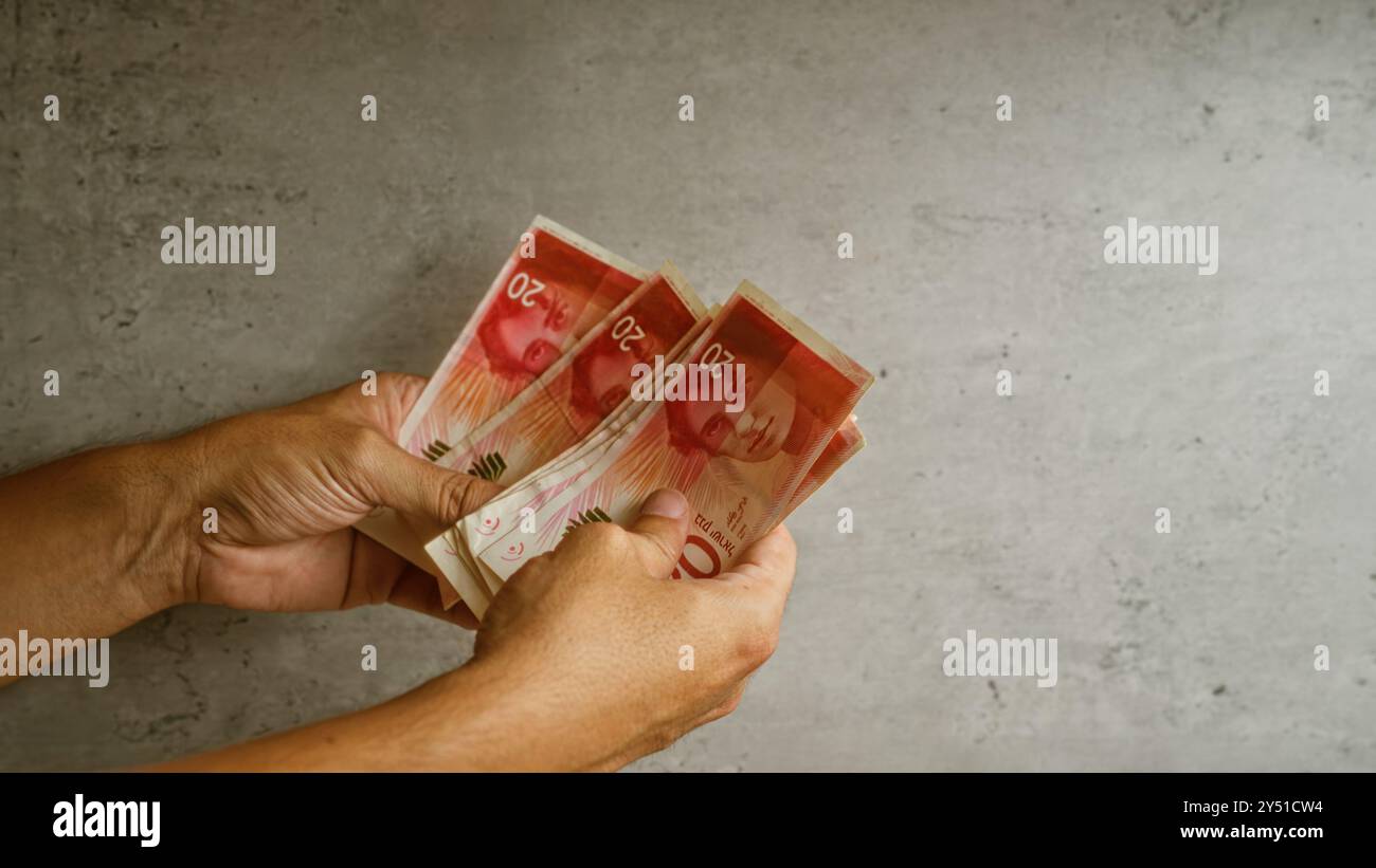 Hands holding israeli shekel banknotes against a concrete background ...