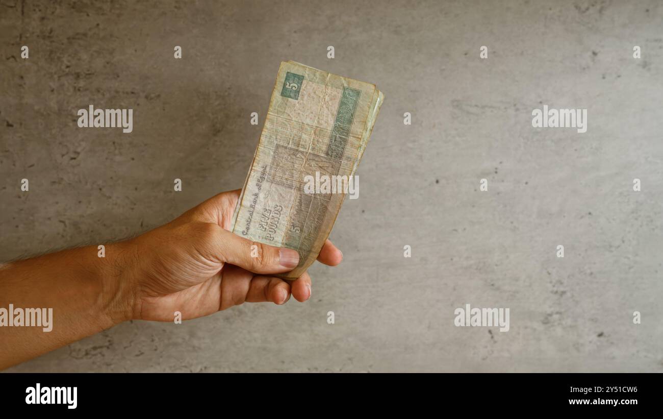 Man holding egyptian pounds against a concrete background with visible ...