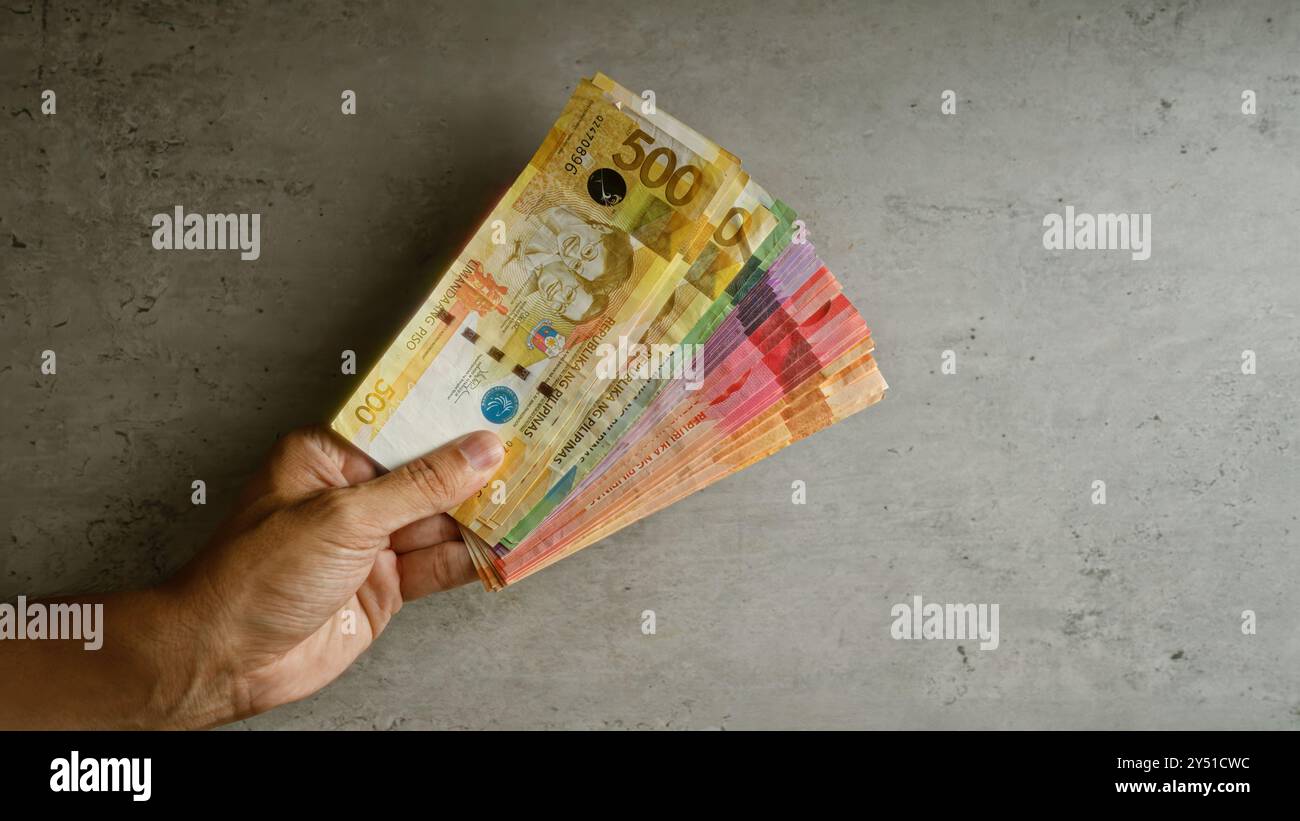 Hand holding a fan of colorful philippine pesos against a concrete ...