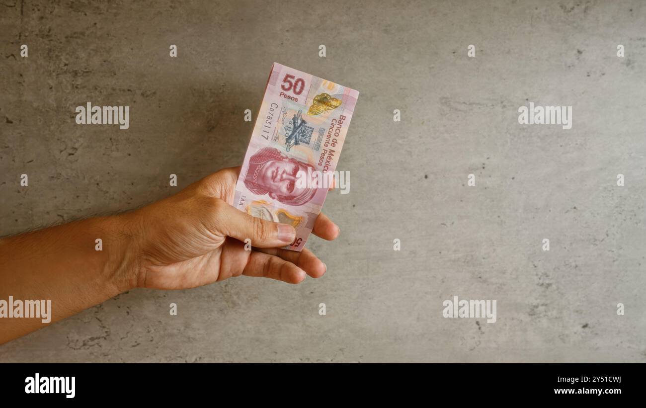Hand holding a 50 peso mexican banknote against a concrete background ...