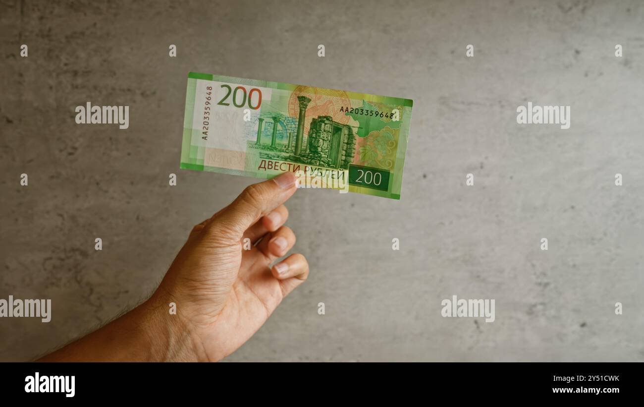 Hand holding russian ruble banknote against concrete wall, focused on ...