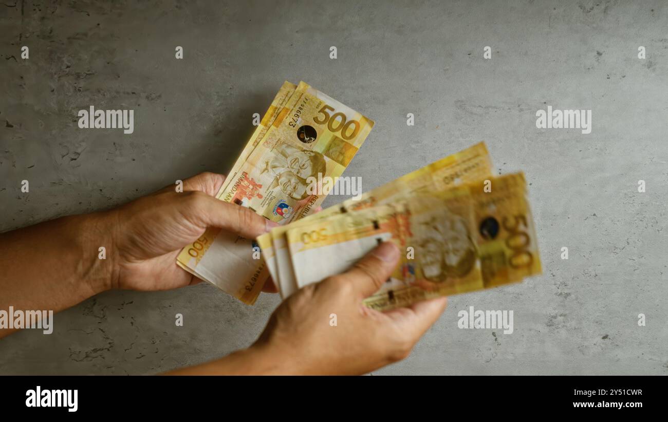 Hands counting philippine pesos with concrete background, highlighting ...