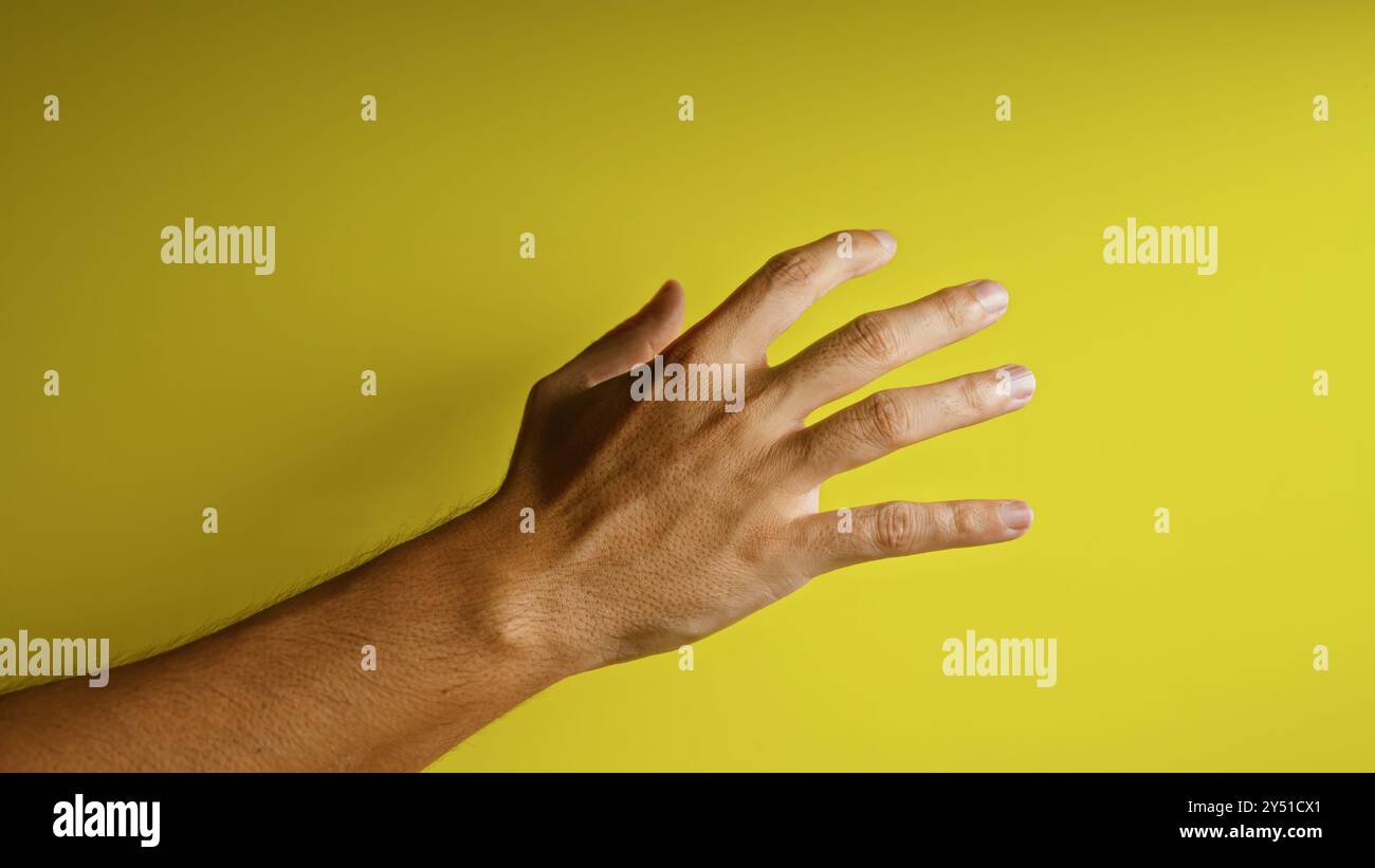 Man's hand reaching out with fingers spread against a bright yellow ...