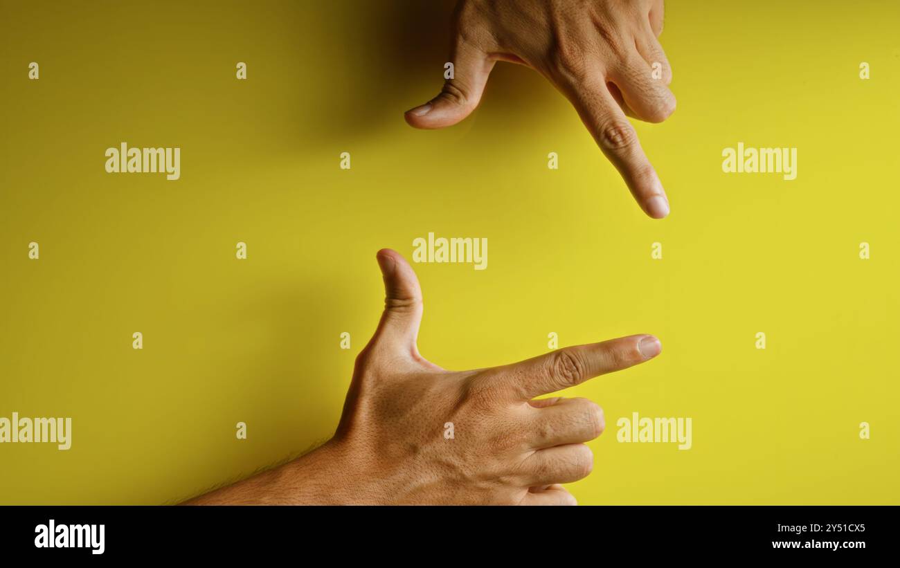 Two hands with fingers forming a frame against a bright yellow ...