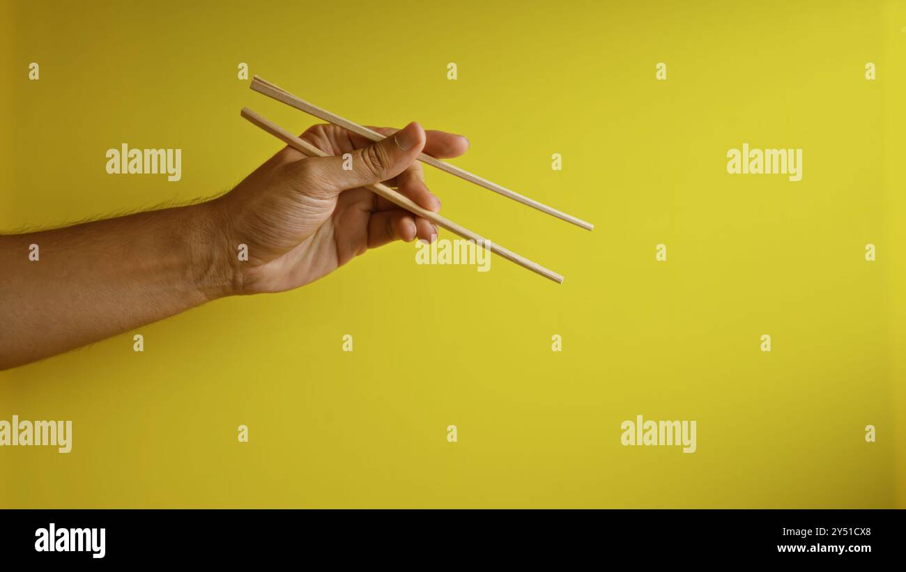 Man holding chopsticks against yellow background showcasing traditional ...