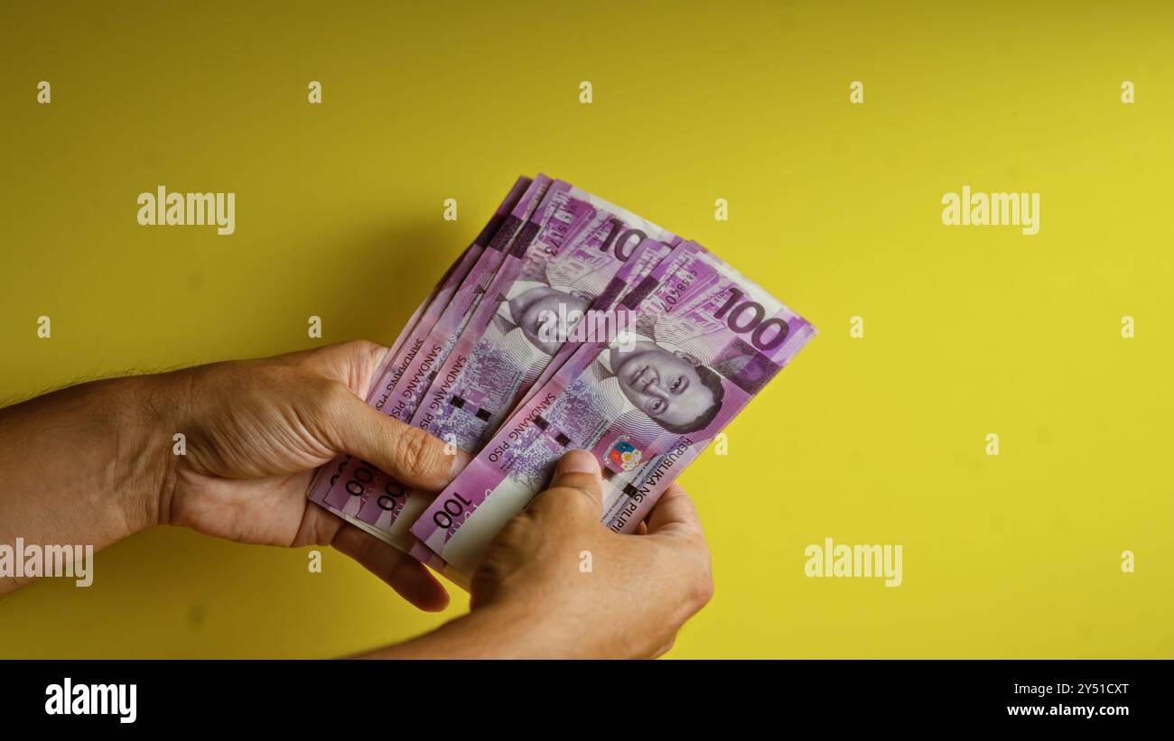 Hand holding several philippine peso bills against a vibrant yellow ...