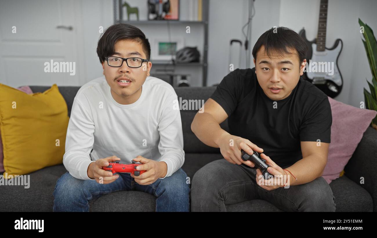 Two asian men focused on playing video games together in a cozy, modern ...