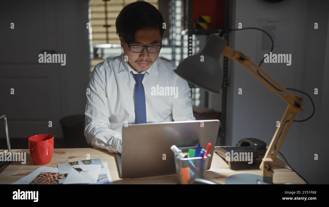 A focused asian man in a white shirt and tie working intently at his ...