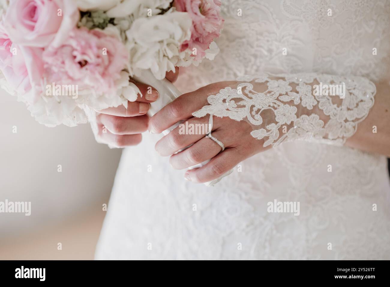 Bride’s hands holding a pink and white bouquet, showing lace and ring ...