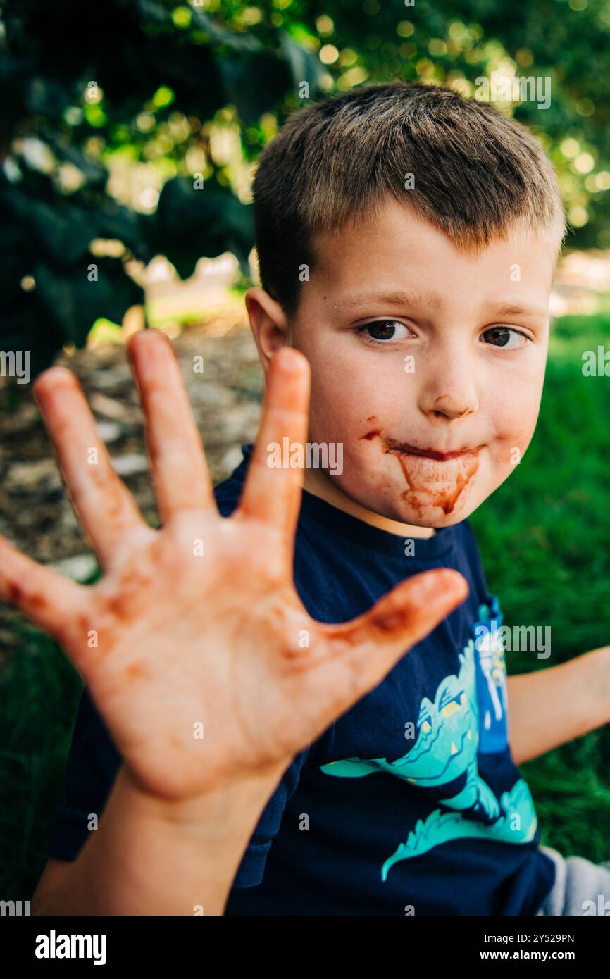 A young boy with a chocolate-covered face holds up his messy hand Stock ...