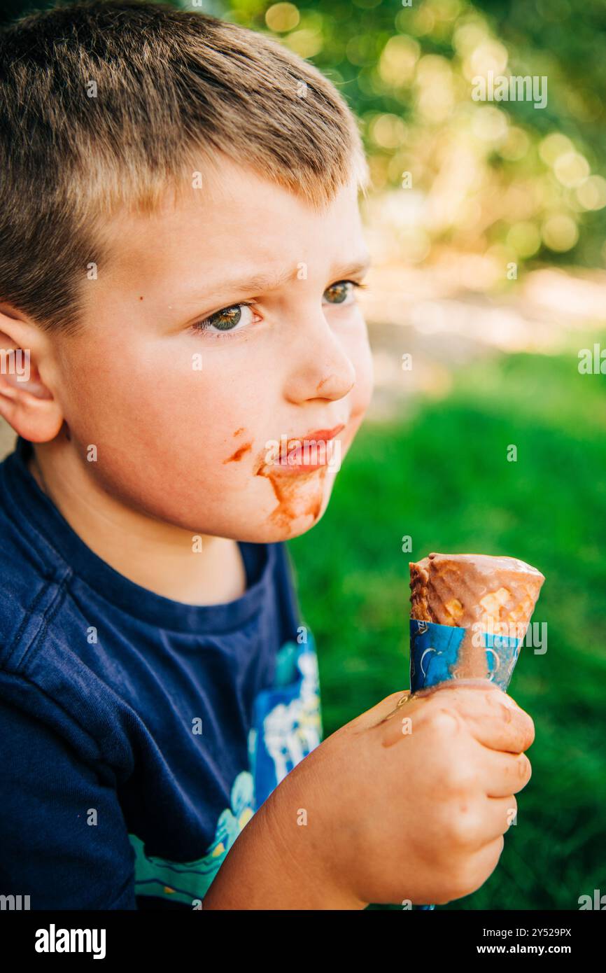 A young boy with a chocolate-stained face holding a melting ice cream ...