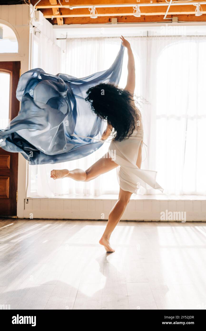 Ballet dancer with flowing blue fabric, in a sunlit studio Stock Photo ...