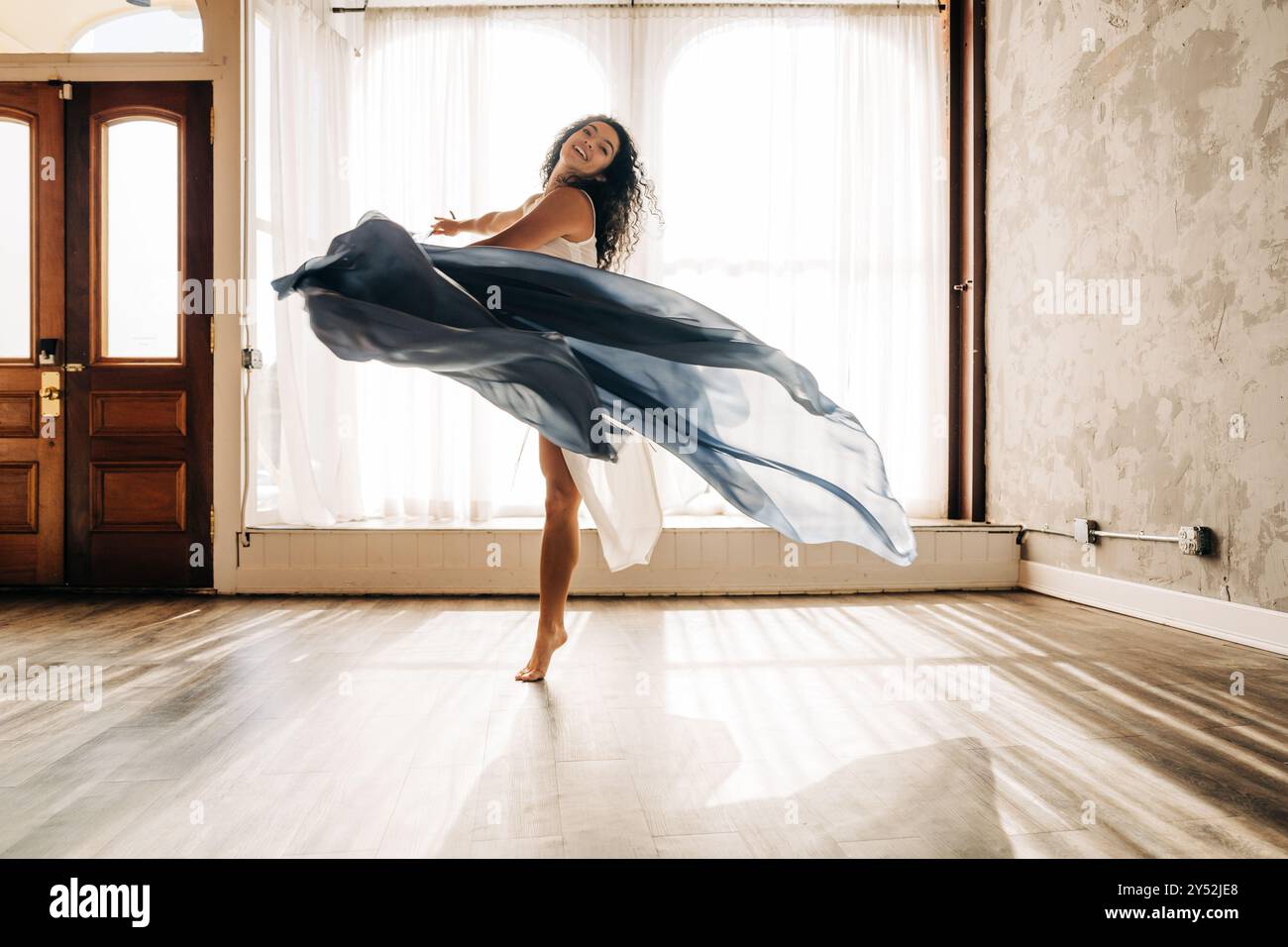 Ballet dancer joyfully spinning with blue fabric in a sunlit studio ...