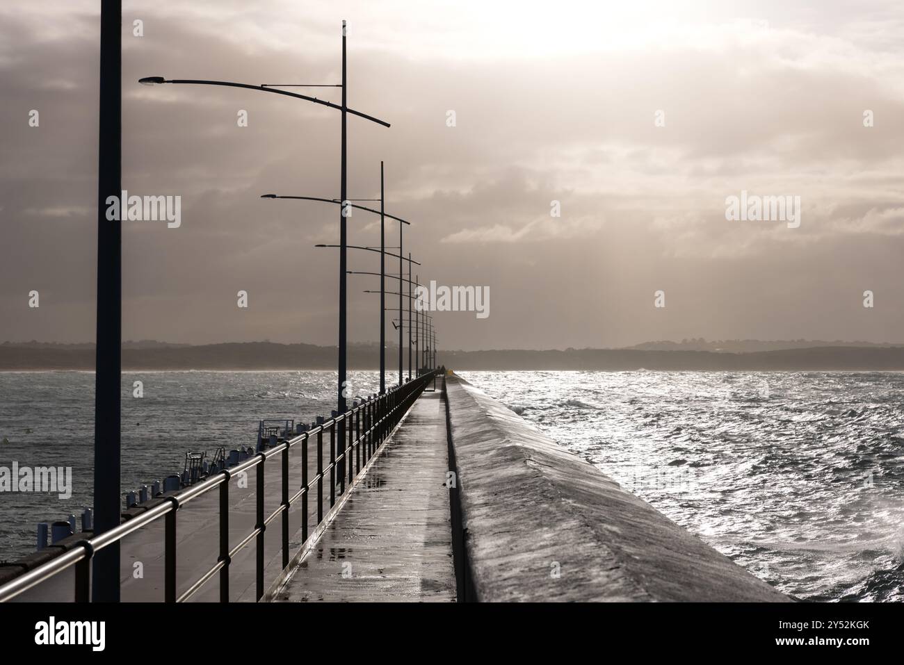 Long pier leading lines to ocean under a cloudy sky, with soft light ...