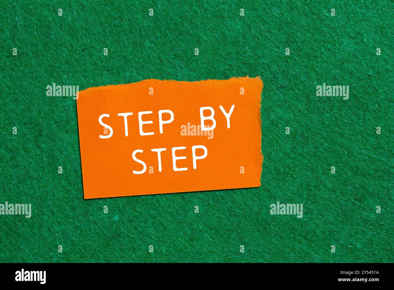 Step by step message written on ripped orange torn paper piece on green background. Conceptual ...