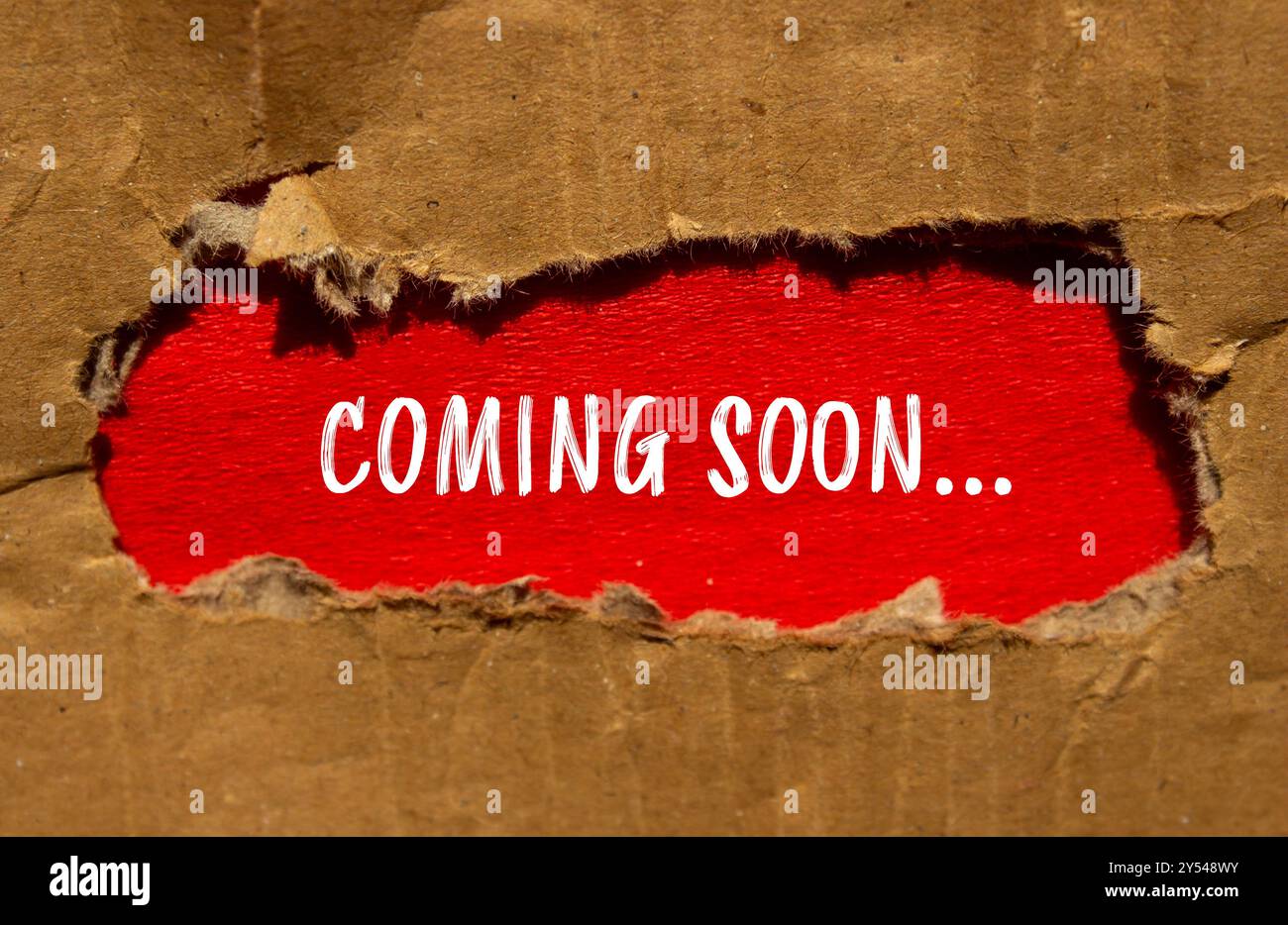 Coming soon message written on torn cardboard paper with red background ...