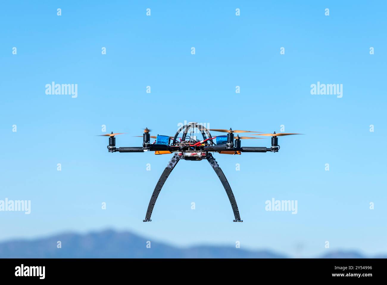 A drone is flying in the sky. The drone is black and has blue batteries ...
