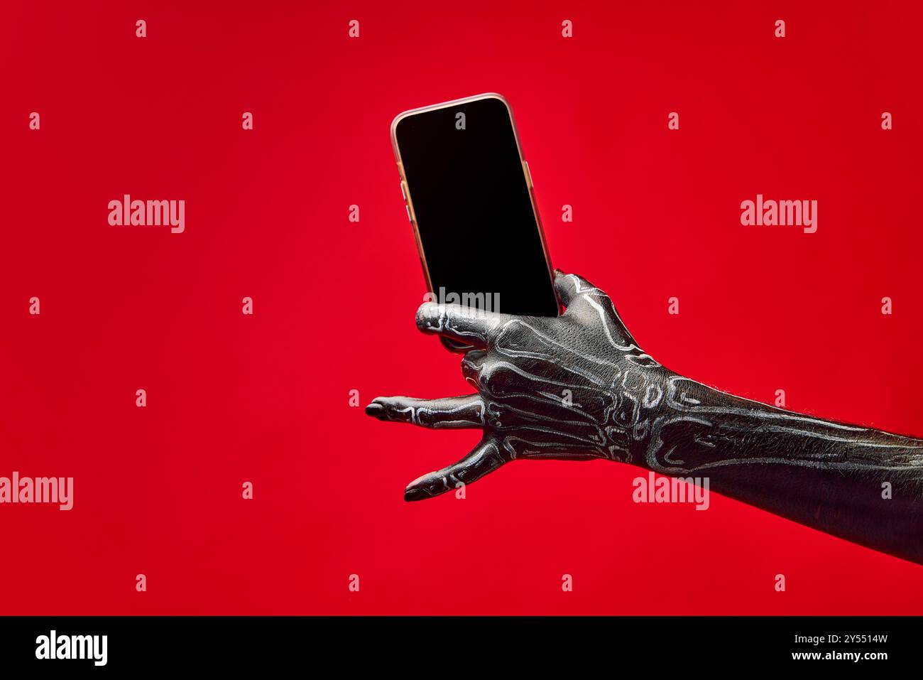 Skeleton hand holding mobile phone against red background. Perfect for ...