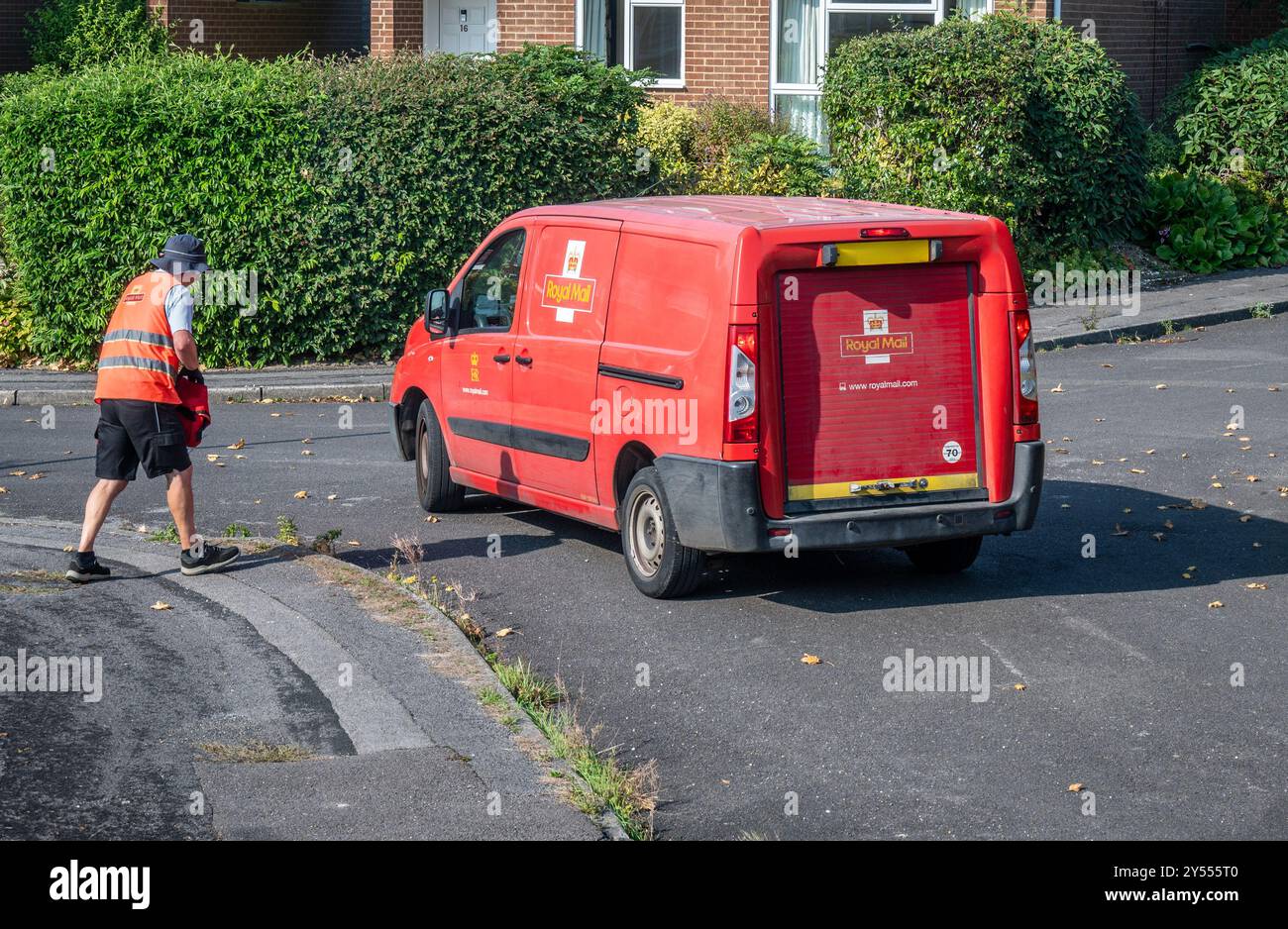 Postman in bright red uniform approaching a postal van having delivered ...