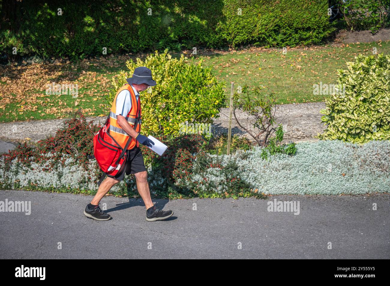 Postman in a bright red uniform delivering letters to homes in England ...