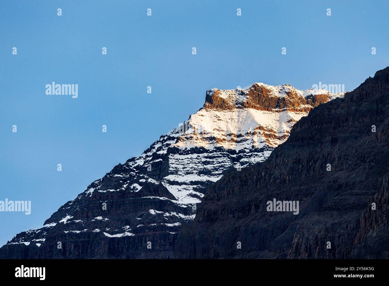 A mountain peak with snow-capped summit against a clear blue sky. The ...