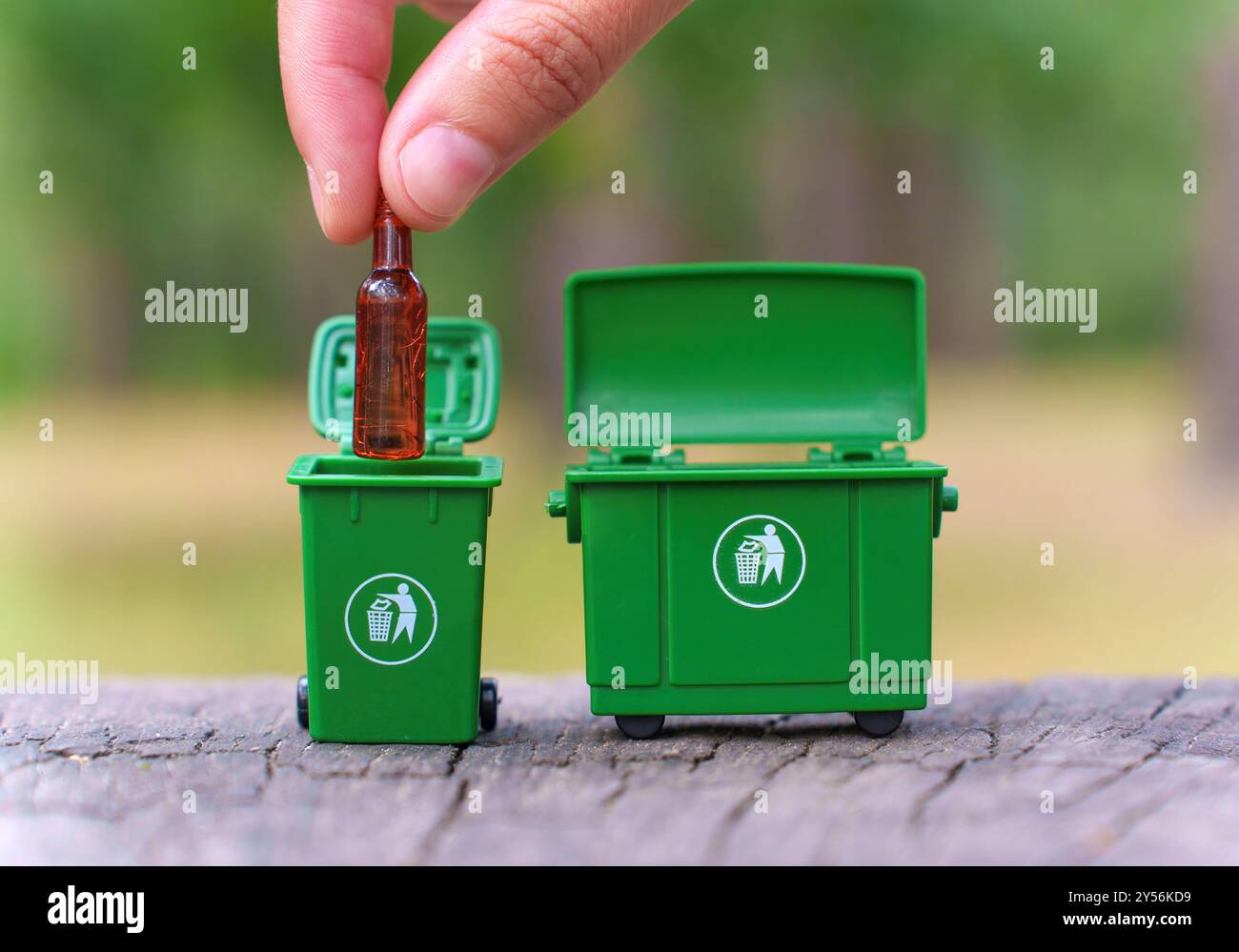 Hand placing a bottle into a miniature green bin next to another open ...