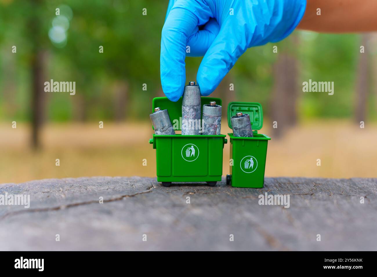 Gloved hand places oxidized batteries into miniature recycling bins set ...