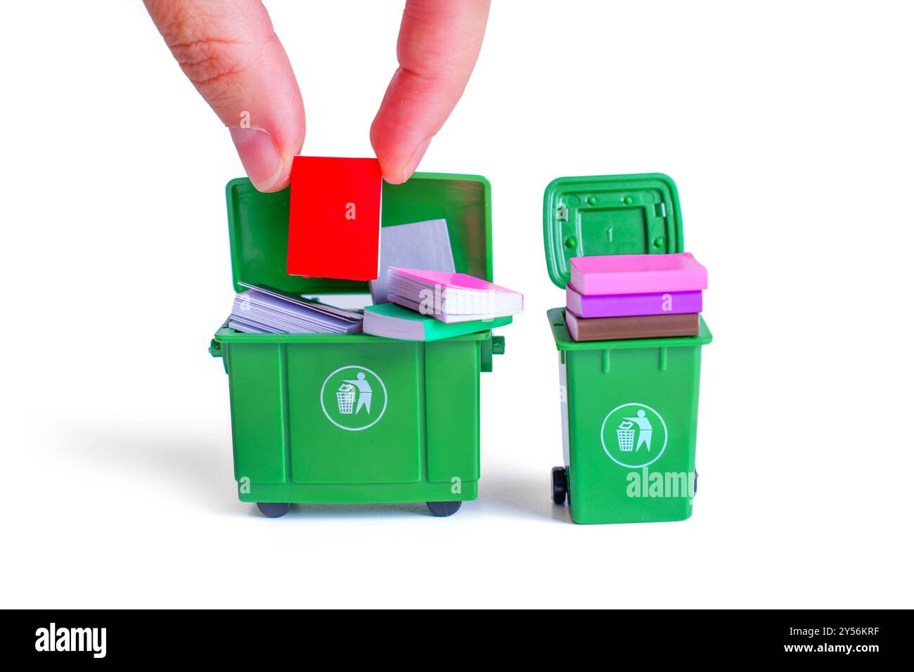 Person's hand putting a red book into a miniature green recycling bin ...