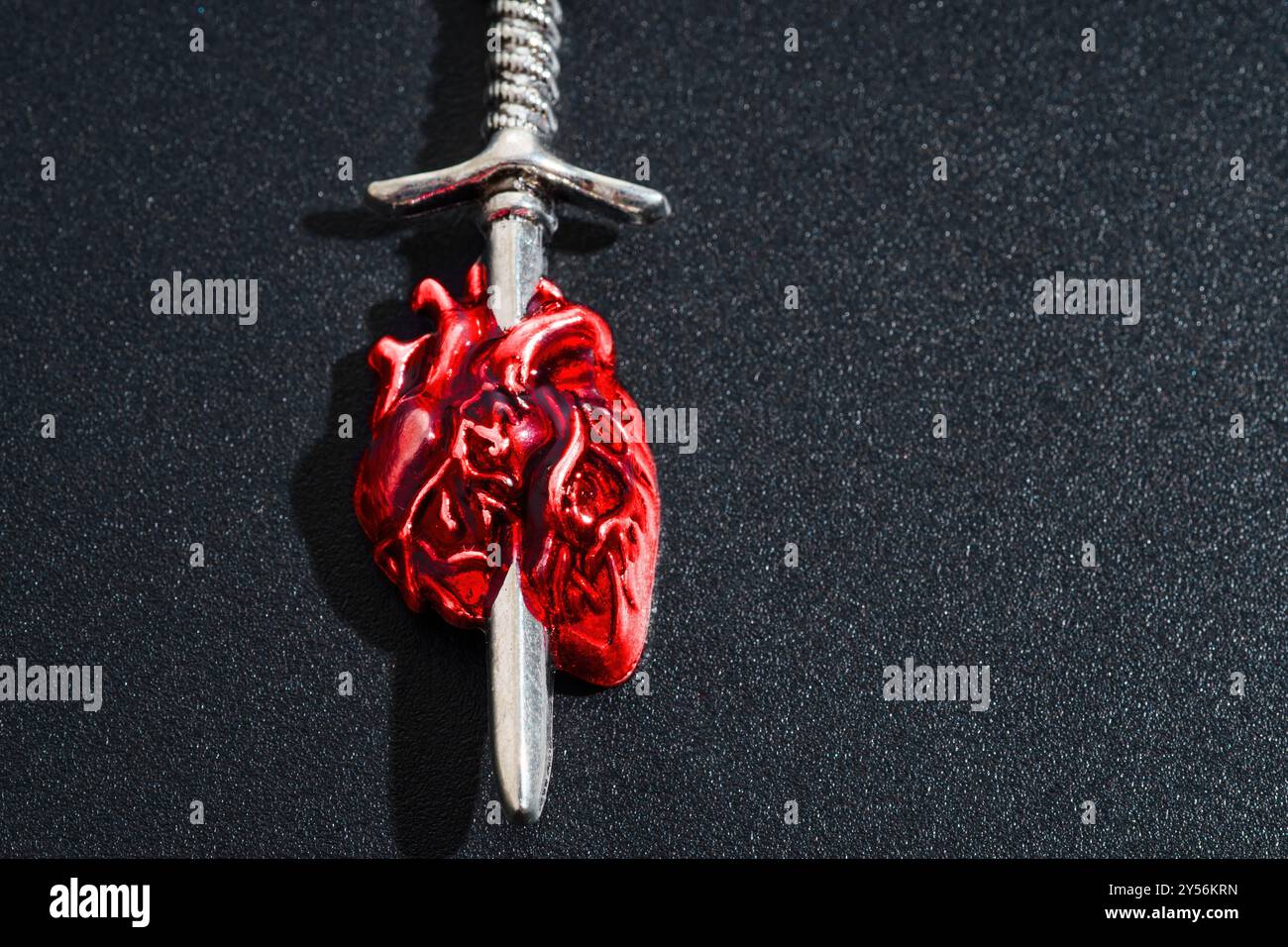 Close-up of a metallic sword piercing a red anatomical heart against a ...