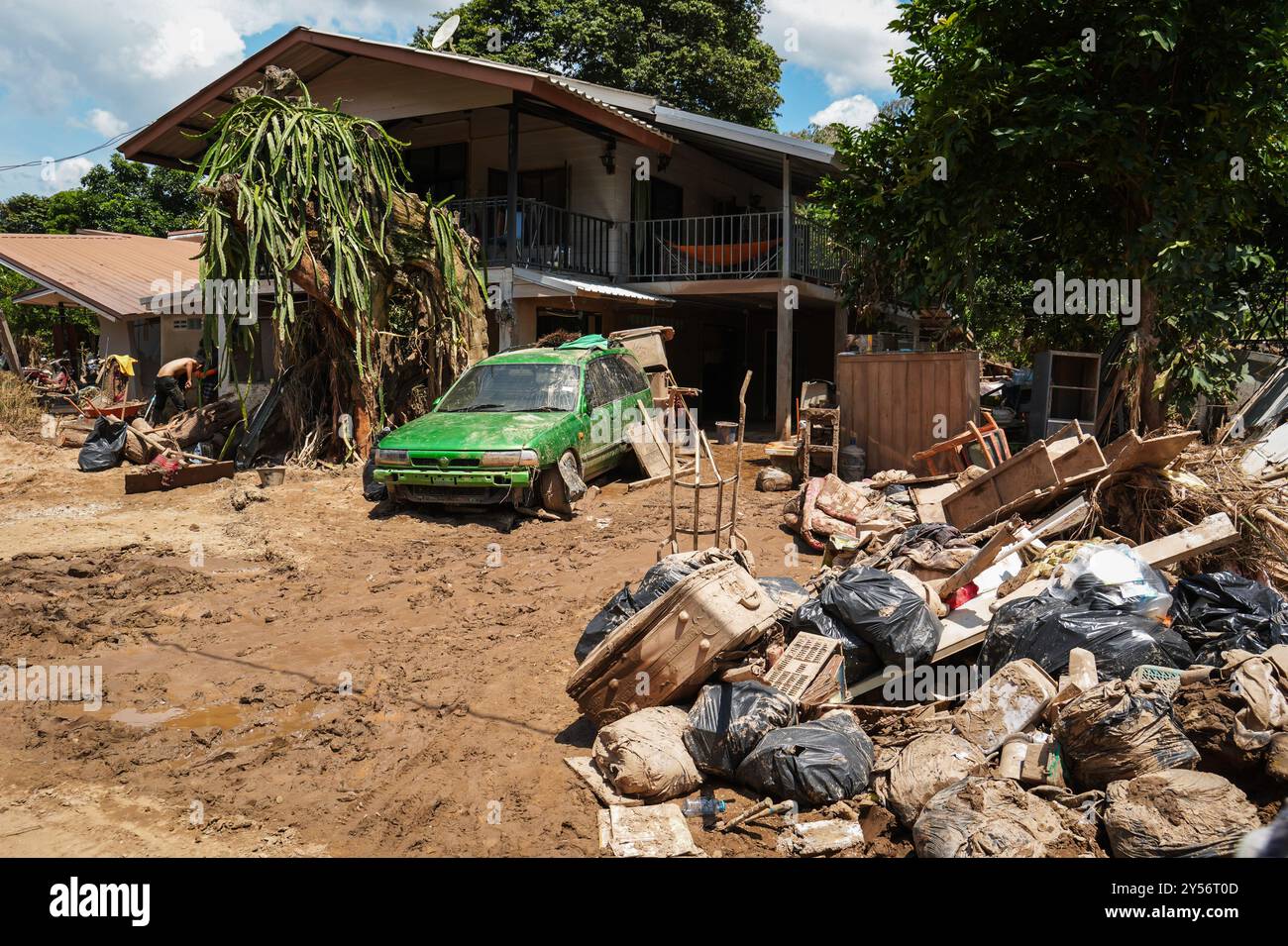A view of a house with a car surrounded by thick mud and debris, after ...