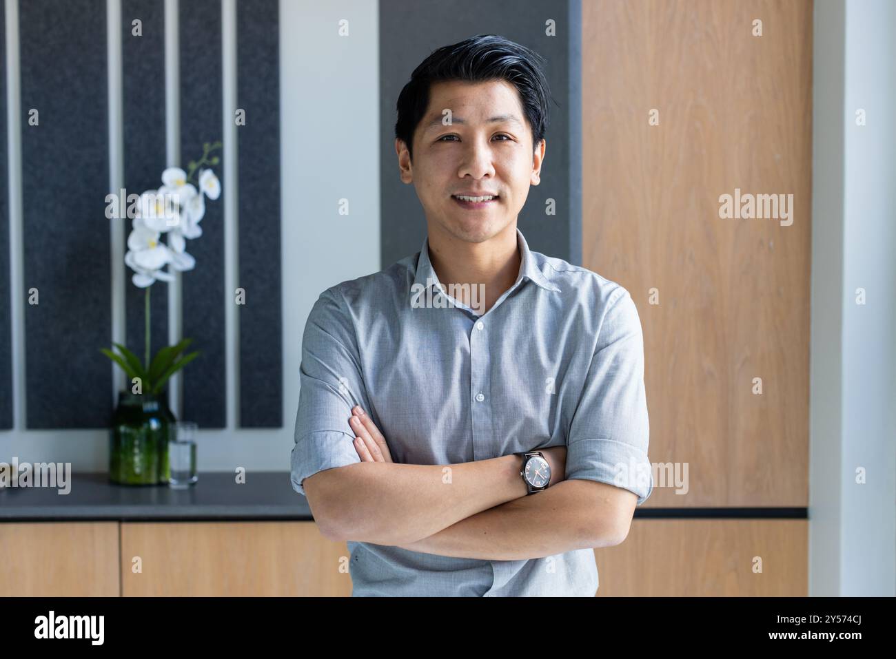 Asian man standing with arms crossed, smiling confidently in office Stock Photo - Alamy