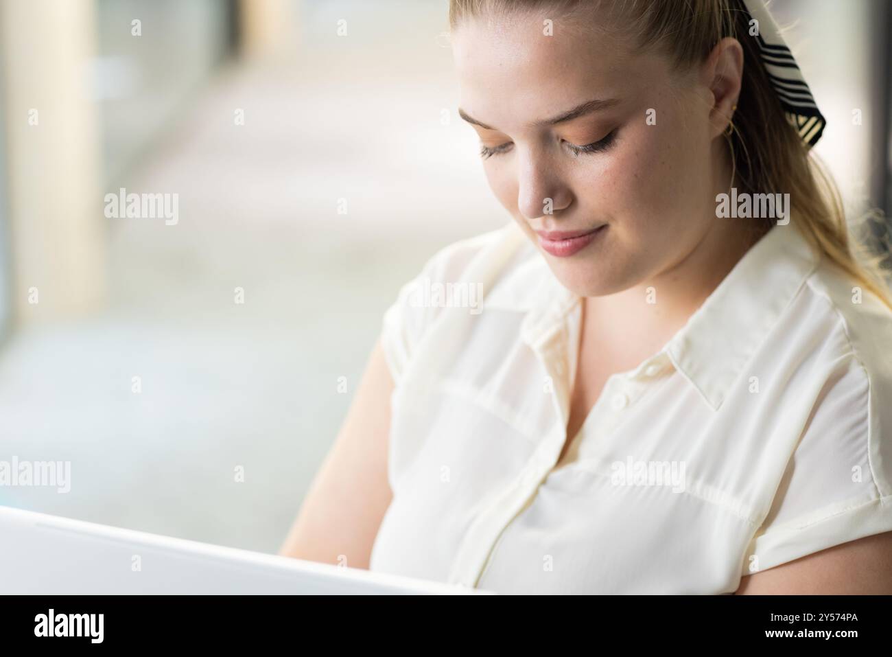 Working on laptop, woman focusing on task in modern office setting ...