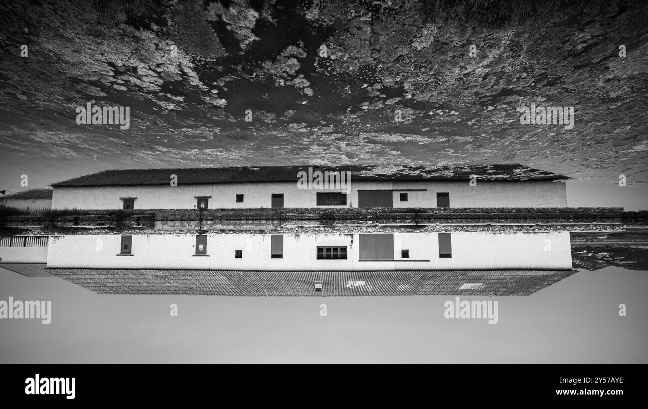 A black and white image of a building reflected in still water ...