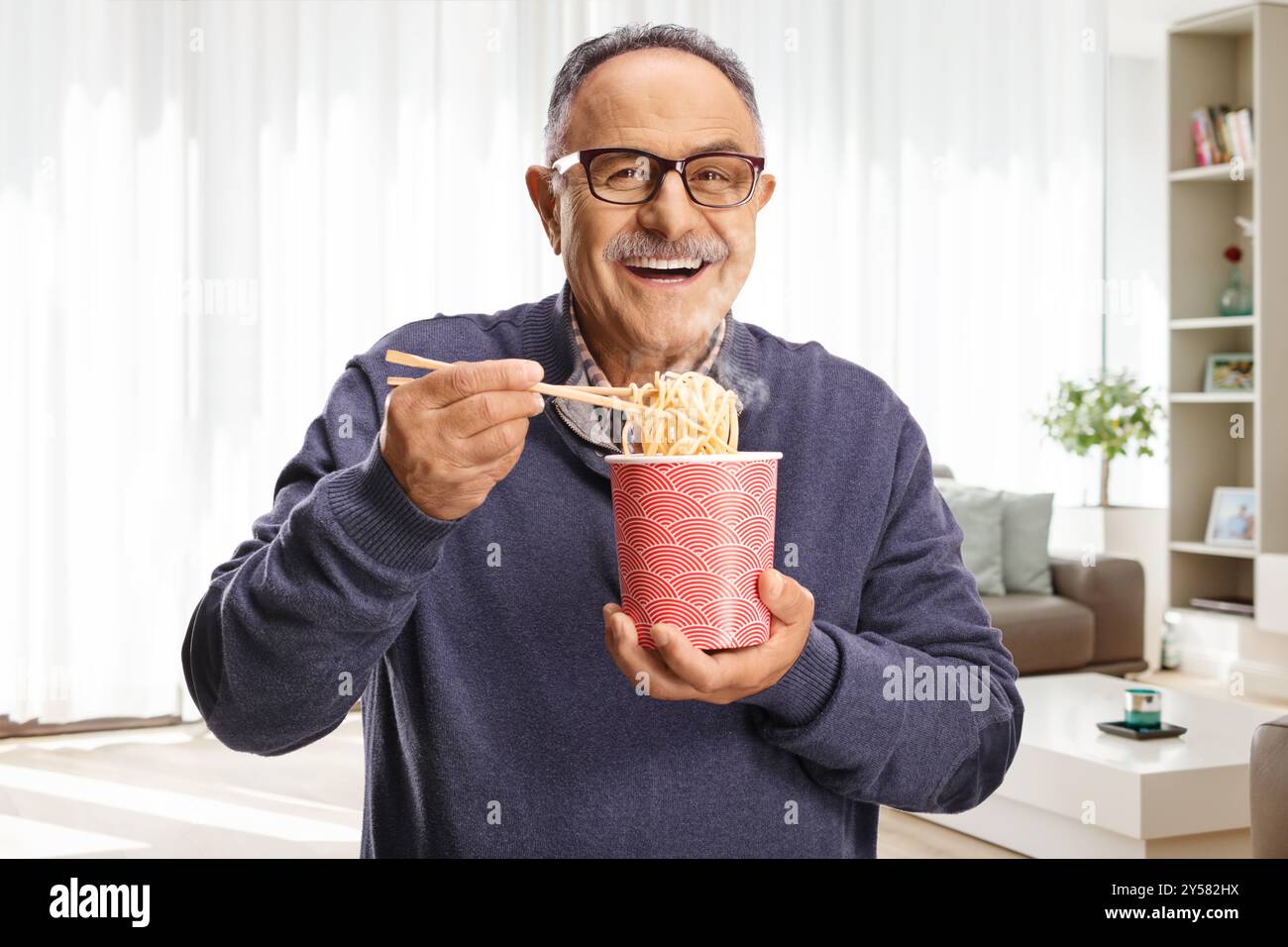 Happy mature man eating noodles from a takeaway box at home Stock Photo ...
