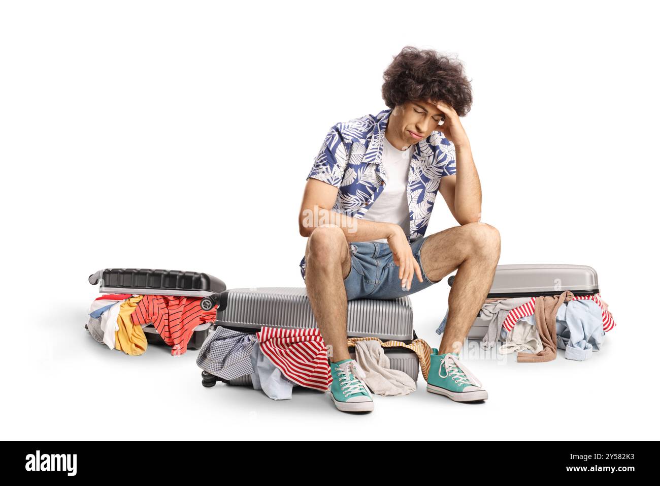 Worried young man sitting on overpacked suitcases isolated on white ...