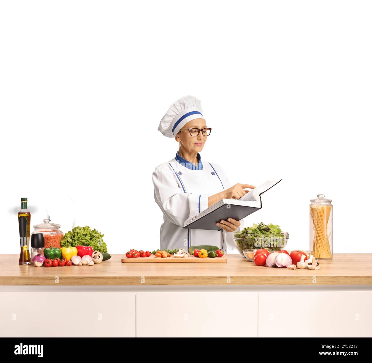 Female chef reading a recipe in a cook book behind a wooden kitchen ...