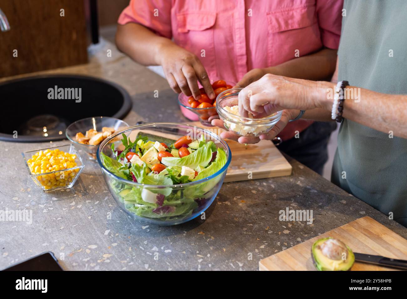 At home, preparing fresh salad, two multiracial female friends adding ...