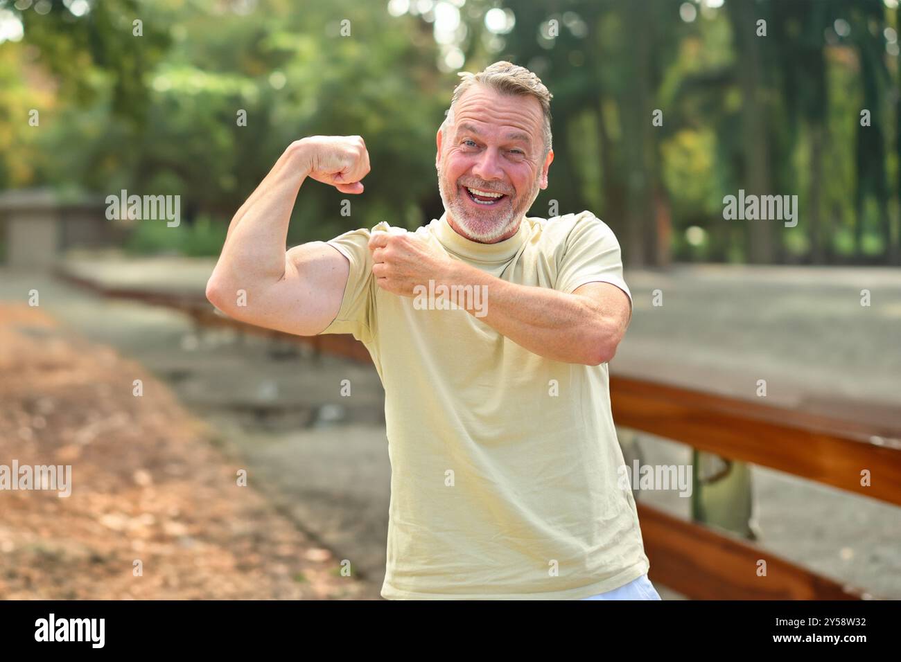 A happy mature man flexing his arm and pointing to his biceps with a ...