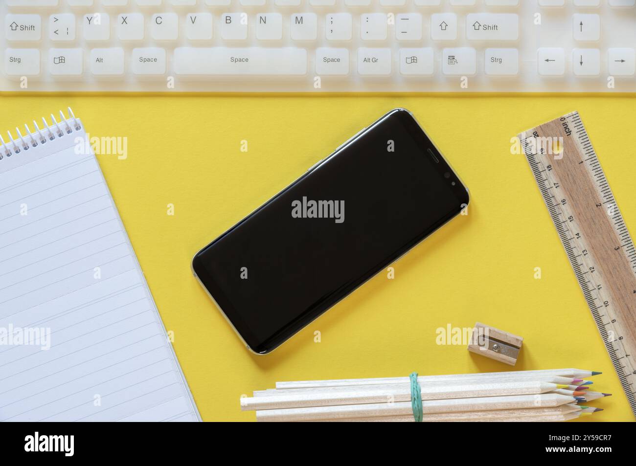 Office desk above view with a black smartphone, white keyboard, and ...