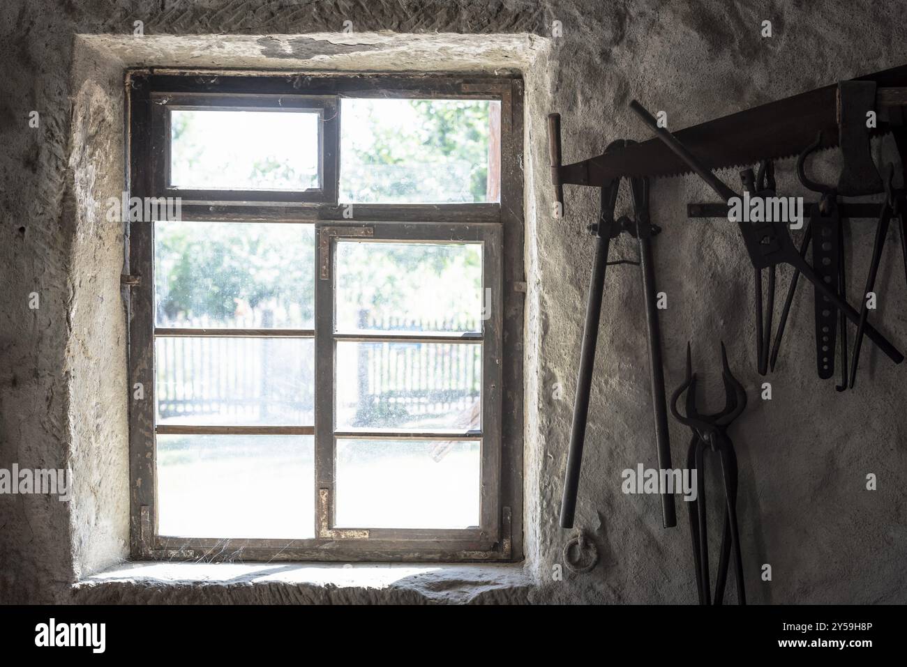Aged window and blacksmith tools hanging on an old wall, in the ...